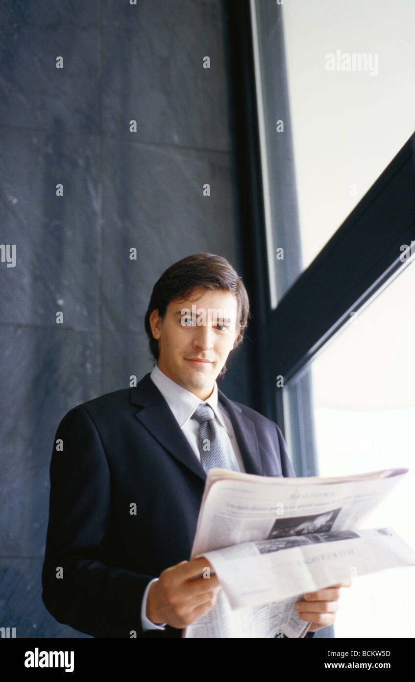 Young businessman holding newspaper, smiling Stock Photo - Alamy