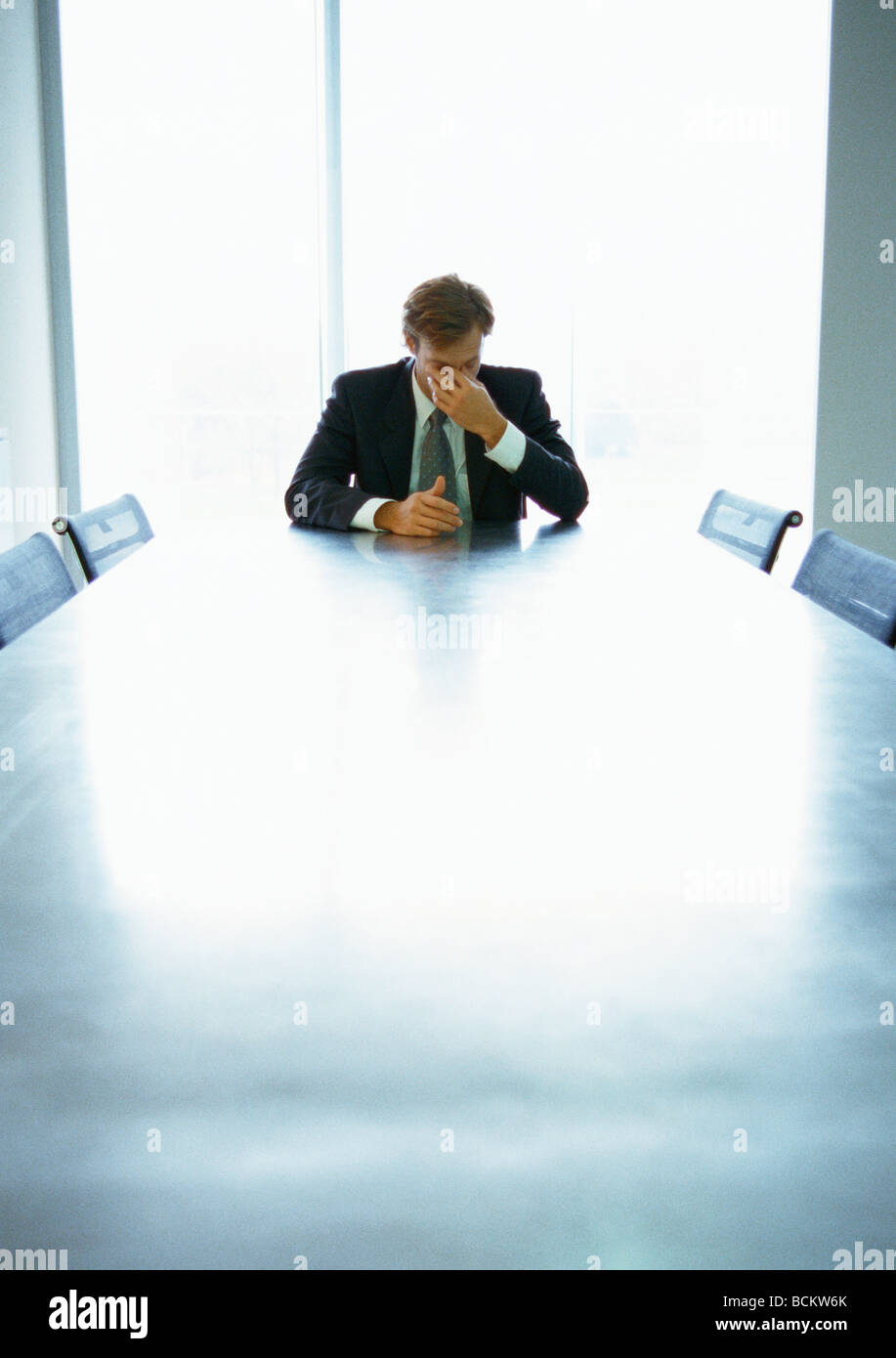 Businessman sitting at conference table, holding head Stock Photo - Alamy
