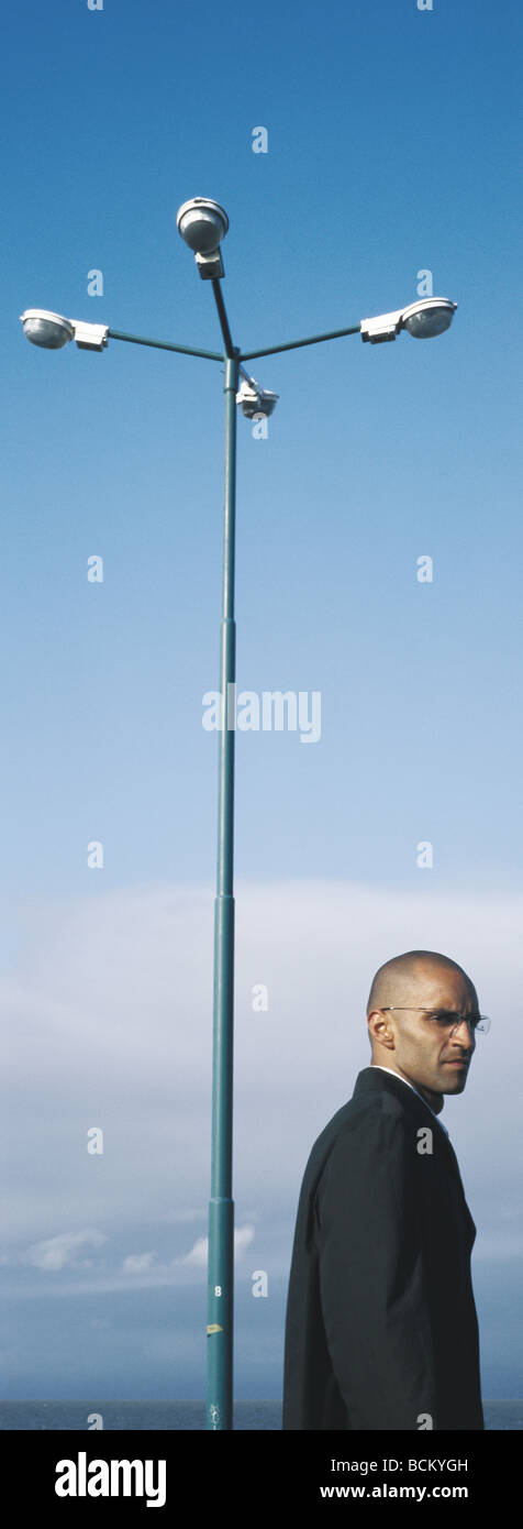 Man standing near lamp post, looking over shoulder Stock Photo - Alamy