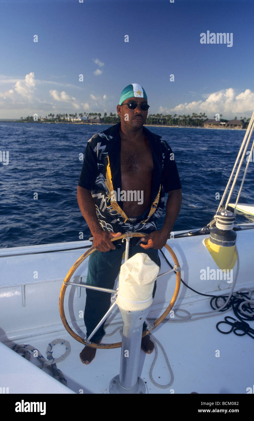 Black sailor man steering at the helm on a catamaran cruise ship ...