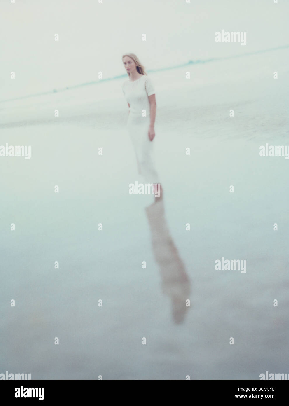 Young female wearing dress, standing ankle deep in water at beach, mid ...