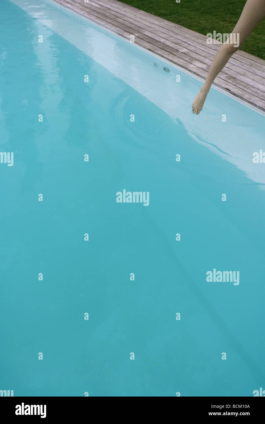 Woman standing next to swimming pool, dipping foot into water, low ...
