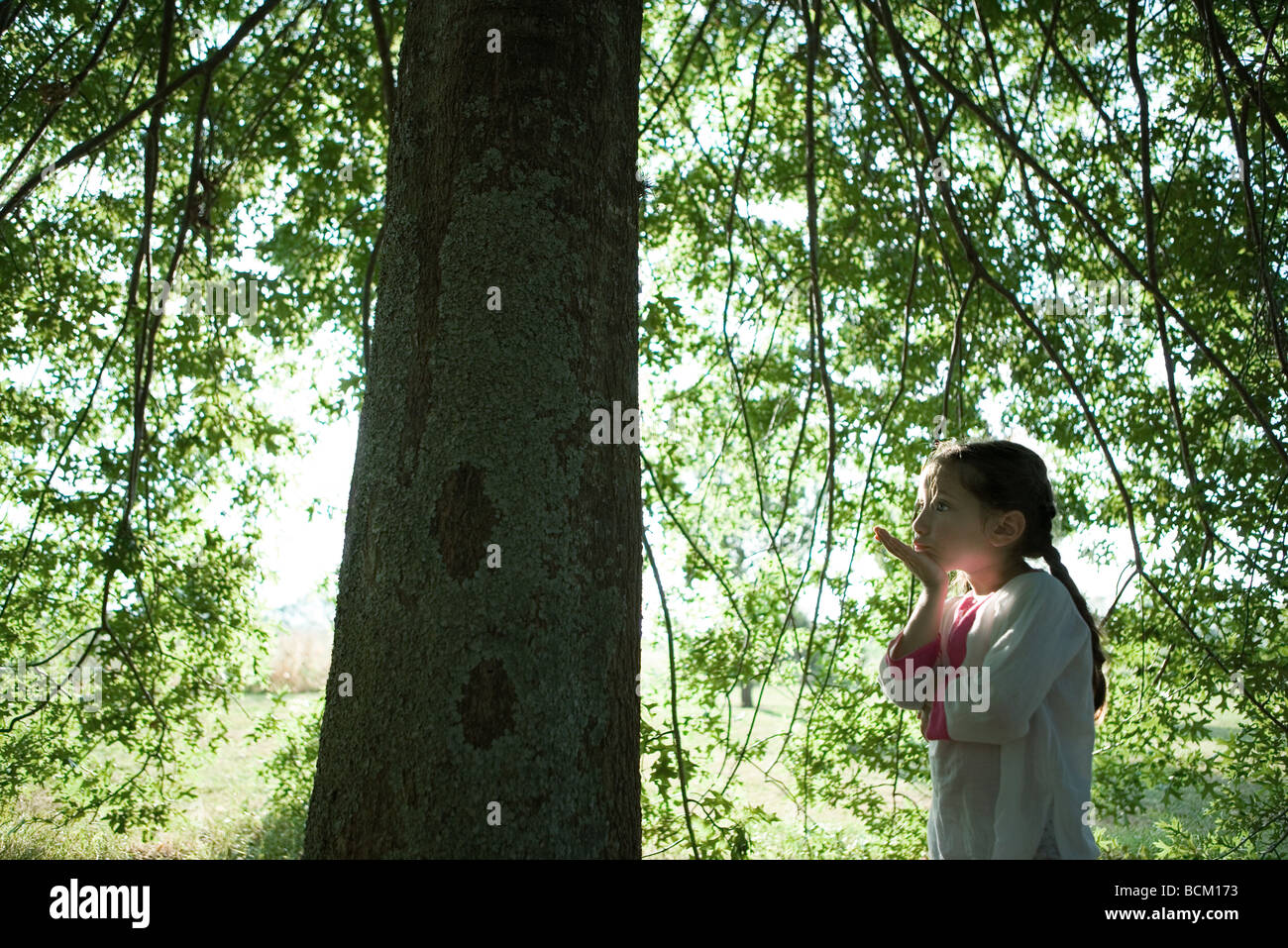 Girl standing under tree, blowing kiss, side view Stock Photo - Alamy