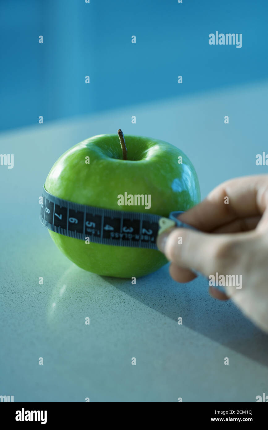 Woman holding measuring tape around apple, cropped view of hand Stock ...