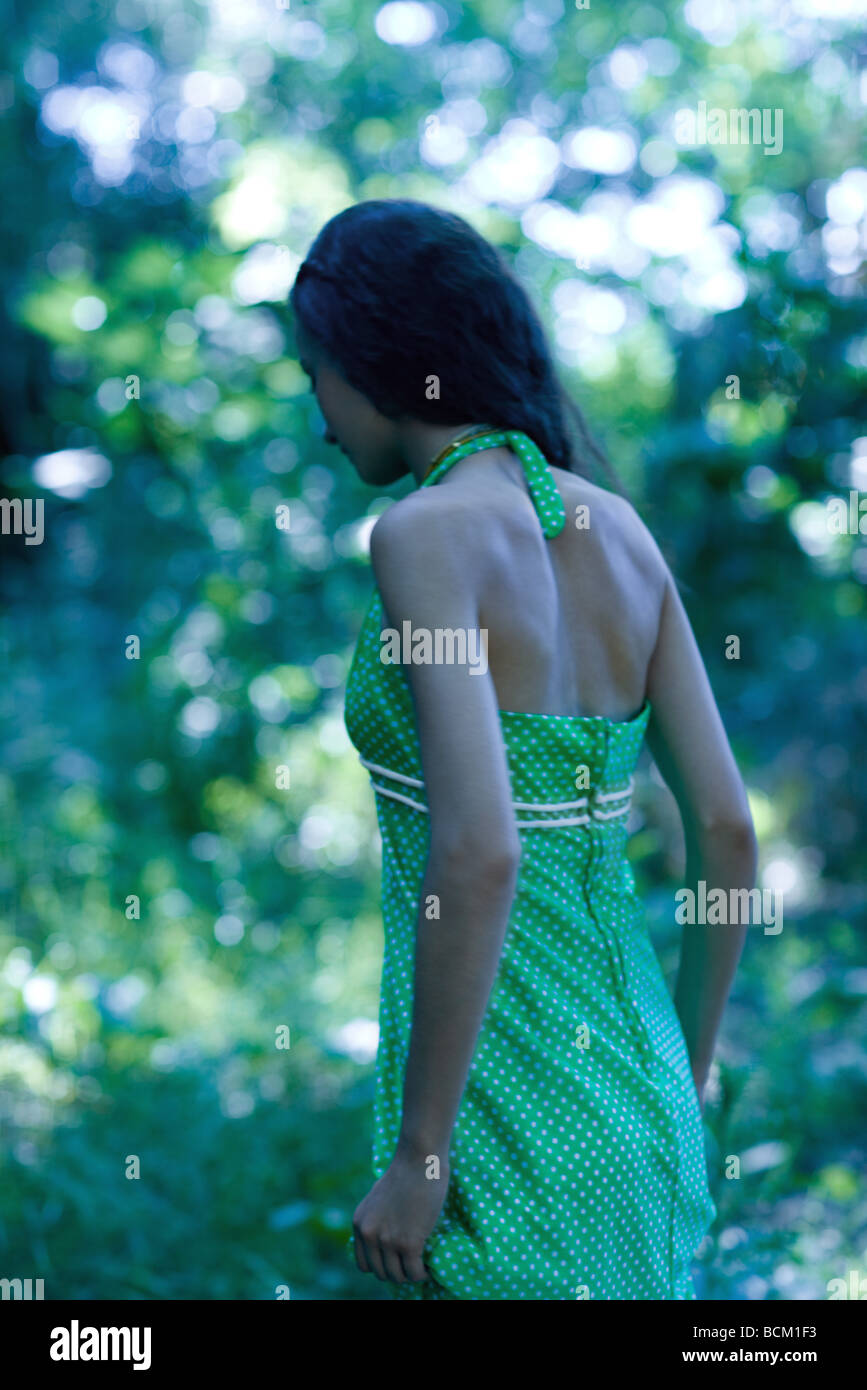 Rear view of a young woman walking through forest, wearing sundress ...
