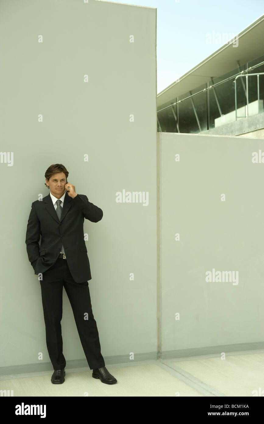 Buisnessman holding cell phone to ear, leaning against wall, full ...