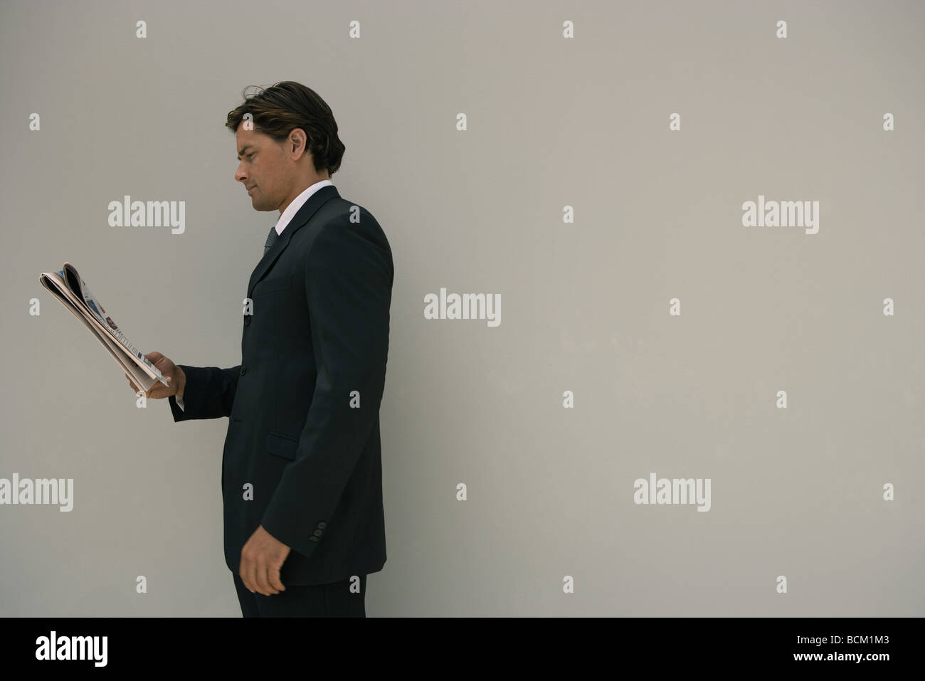 Businessman standing, reading newspaper, side view Stock Photo - Alamy