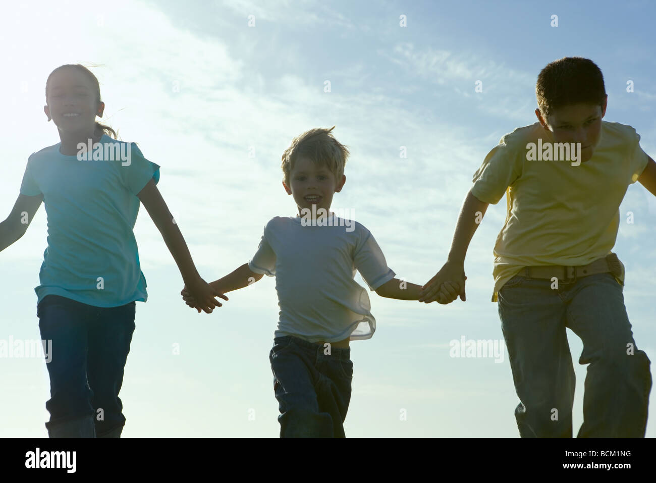 Three children running, holding hands, backlit Stock Photo - Alamy