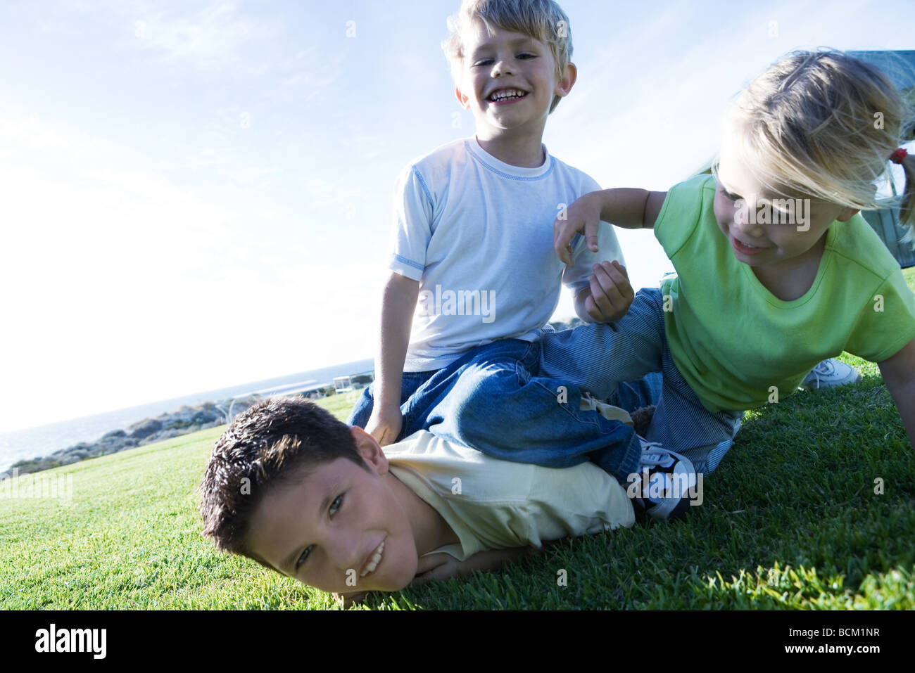 Three children wrestling on grass, smiling Stock Photo - Alamy