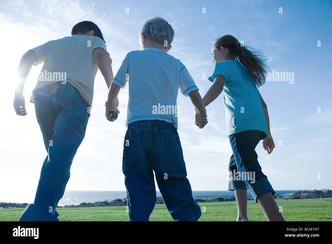 Three children walking across grass, holding hands, low angle view ...