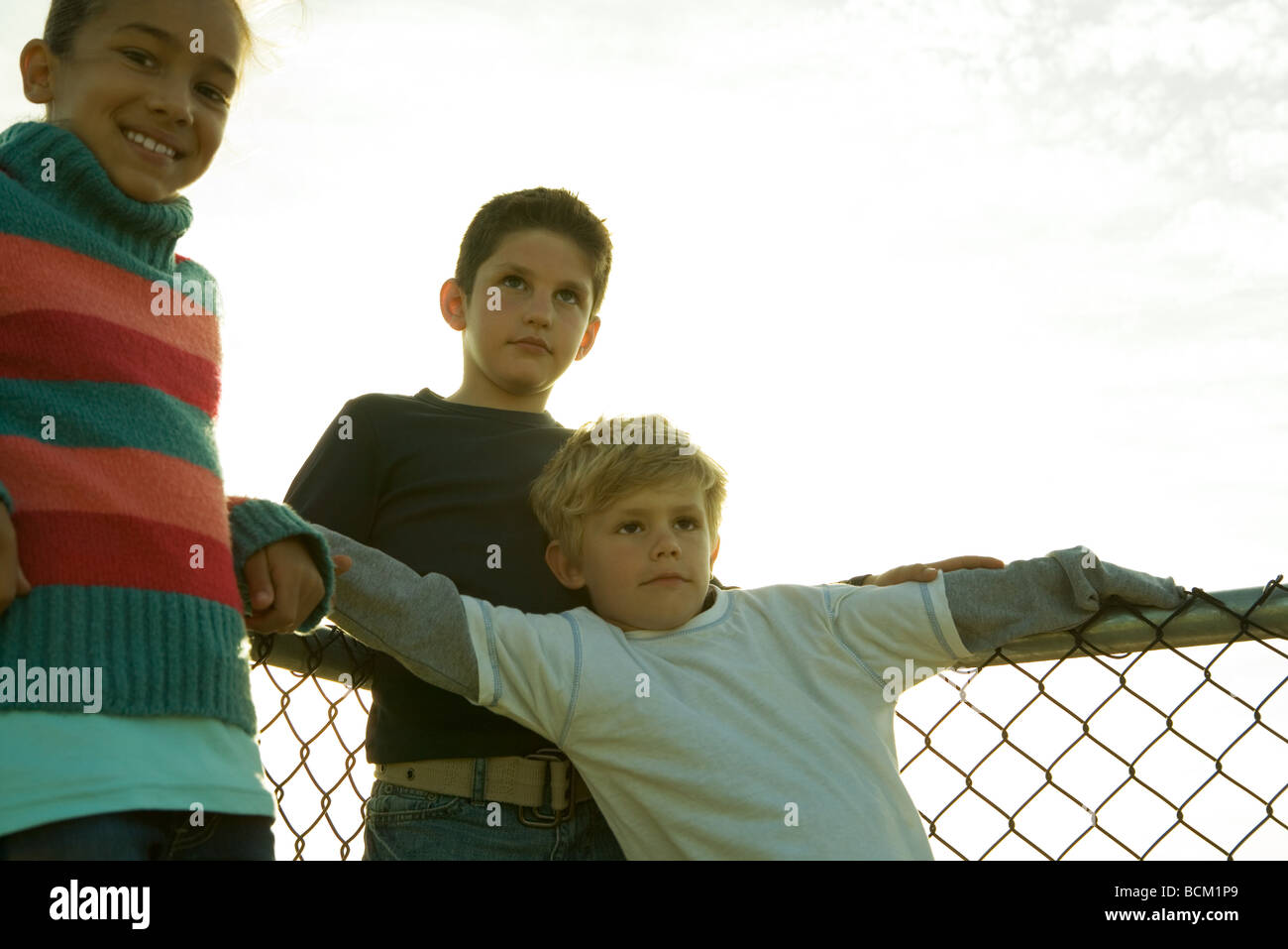 Three children leaning against chainlink fence, low angle view Stock ...