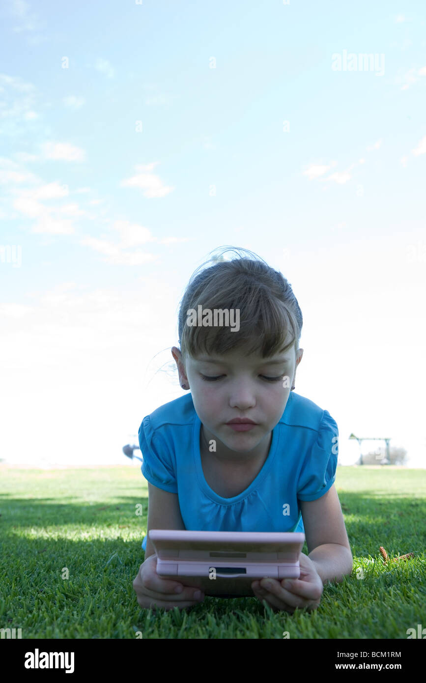Girl lying on grass, playing with video game, front view Stock Photo ...