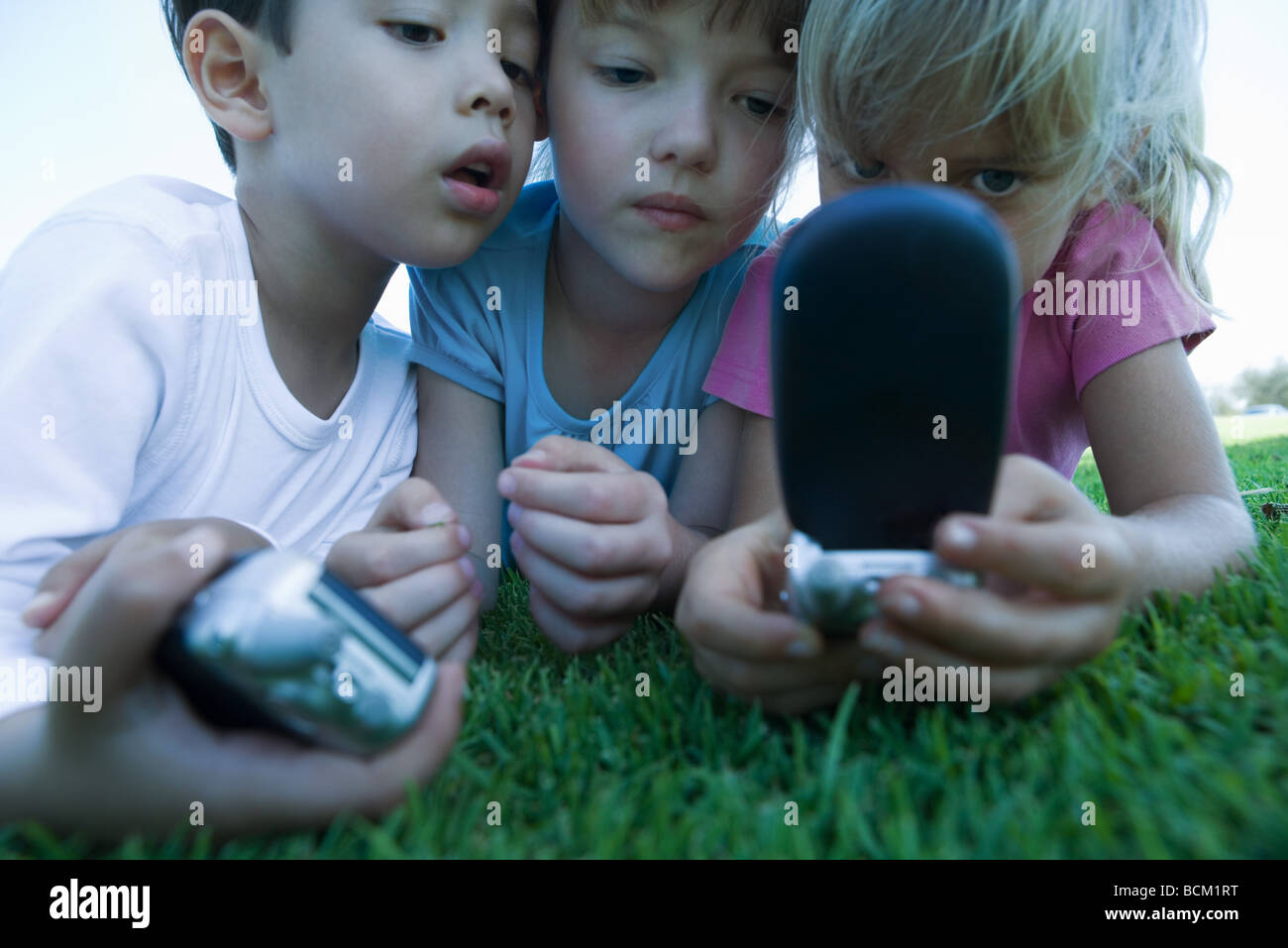 Three children lying on grass, using cell phones, close-up Stock Photo ...