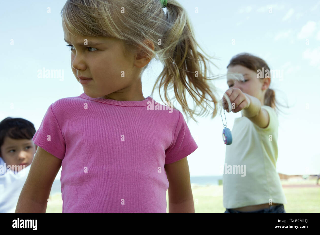 Three children outside, girl in foreground turning head while girl in ...