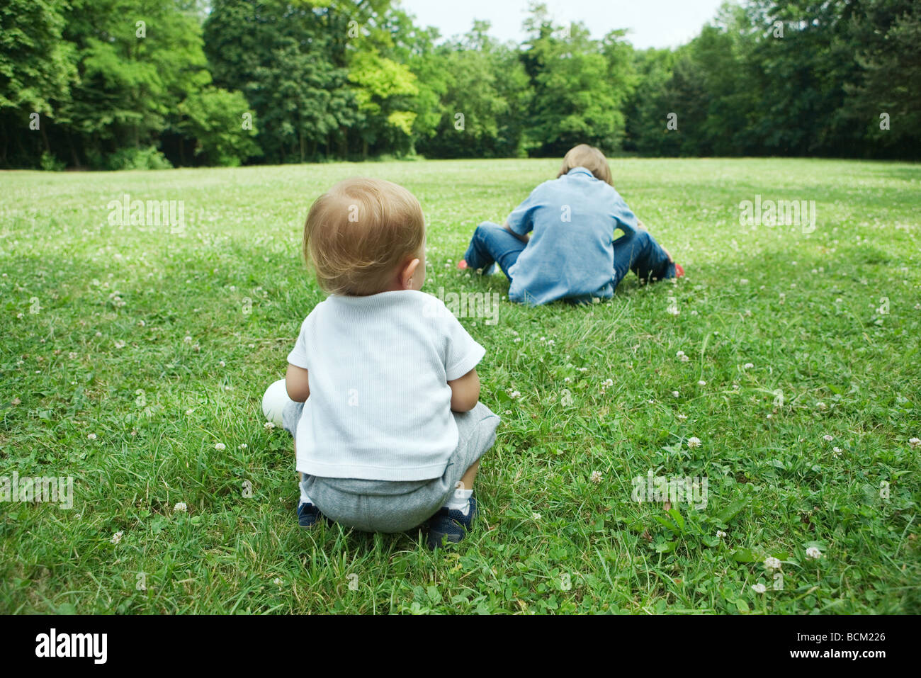 Baby boy crouching in grass, watching older sibling, rear view Stock ...