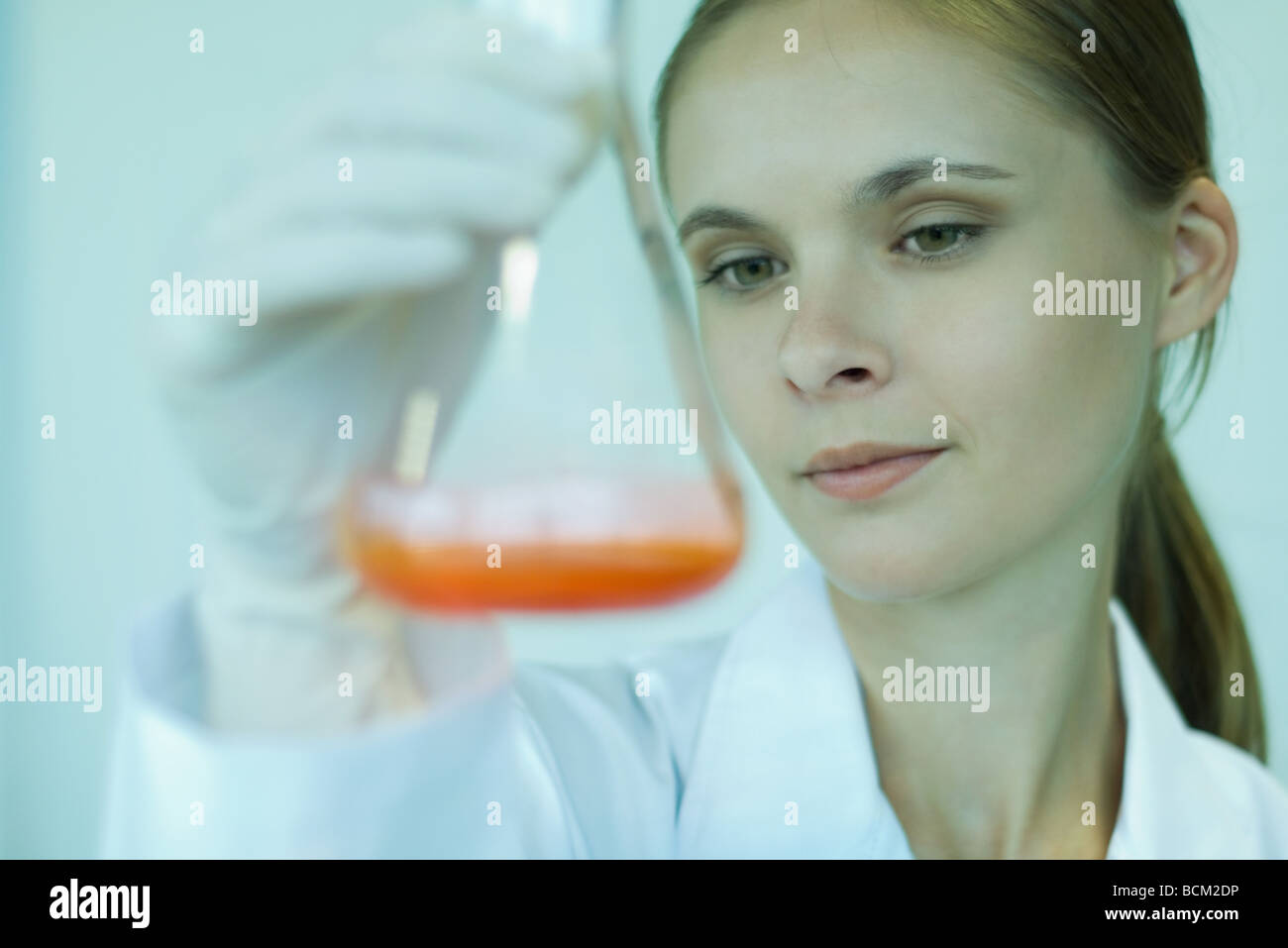 Female scientist holding up beaker with liquid inside, looking down ...