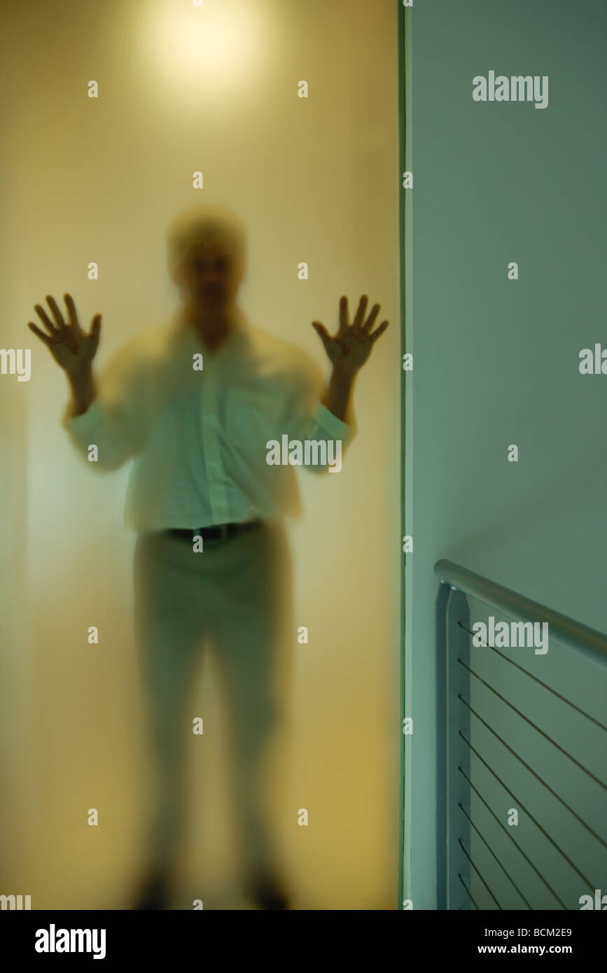Man standing behind window, hands pressed against glass, looking ...