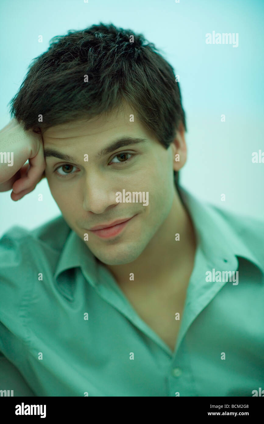 Young man leaning head on hand, smiling at camera, portrait Stock Photo ...