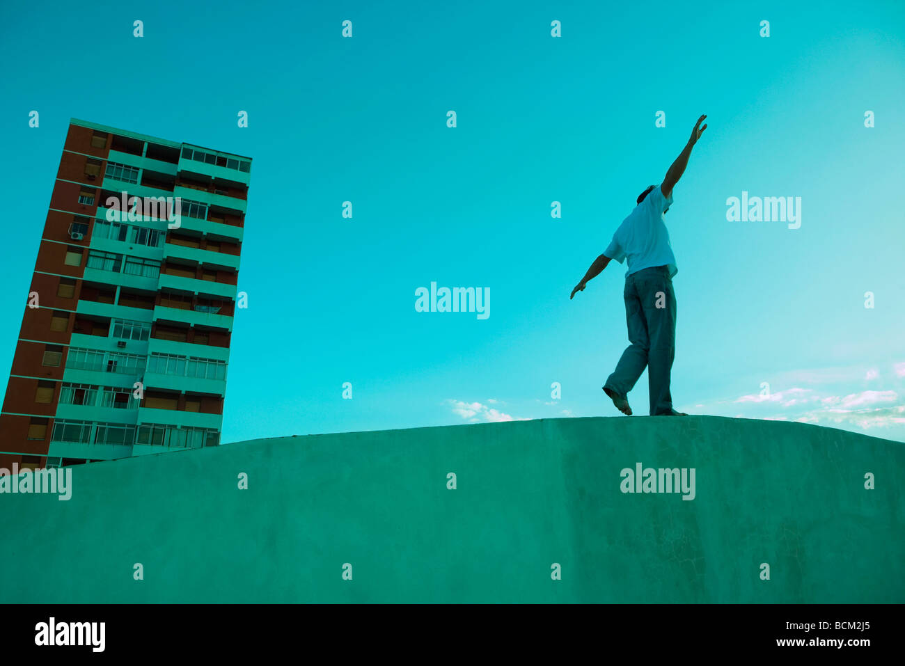 Man walking along ledge with arms out, high rise apartment building in ...
