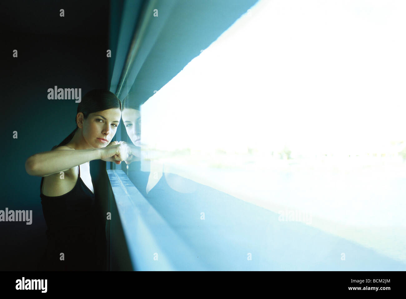 Woman standing with fists pressed against window, looking at camera ...