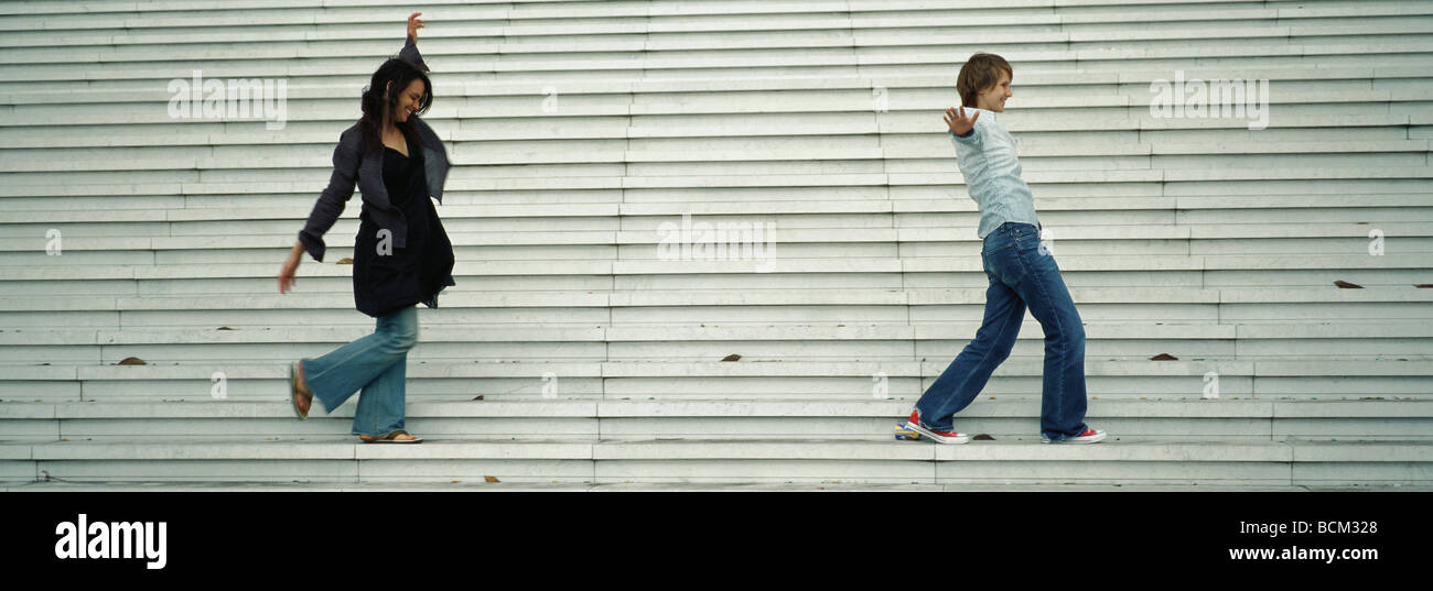 Two young friends walking on steps, arms out, side view Stock Photo - Alamy
