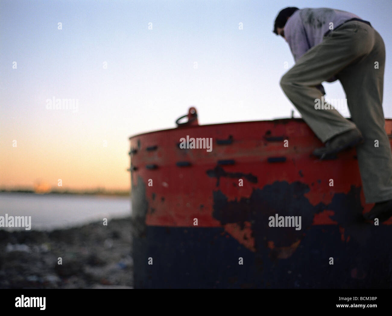 Young man climbing onto metal tank, rear view Stock Photo - Alamy