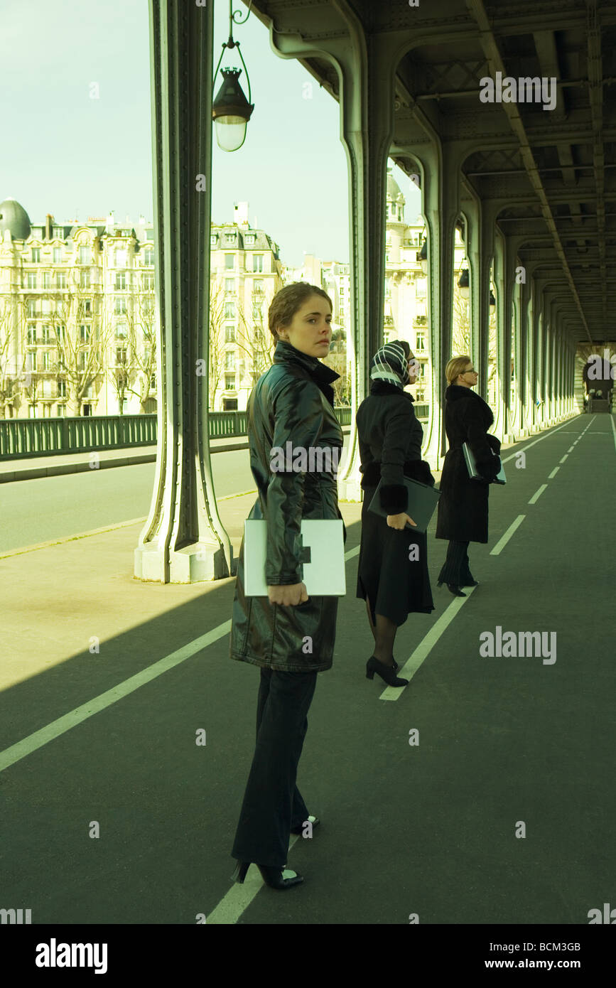 Three women walking in urban setting, all carrying laptop computers ...