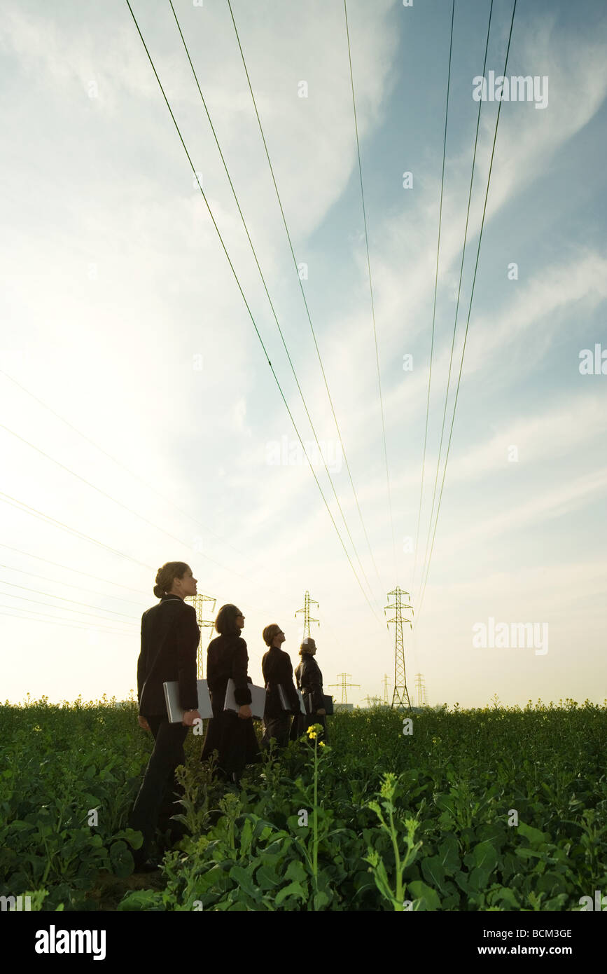 Four businesswomen walking in field, all carrying laptop computers ...