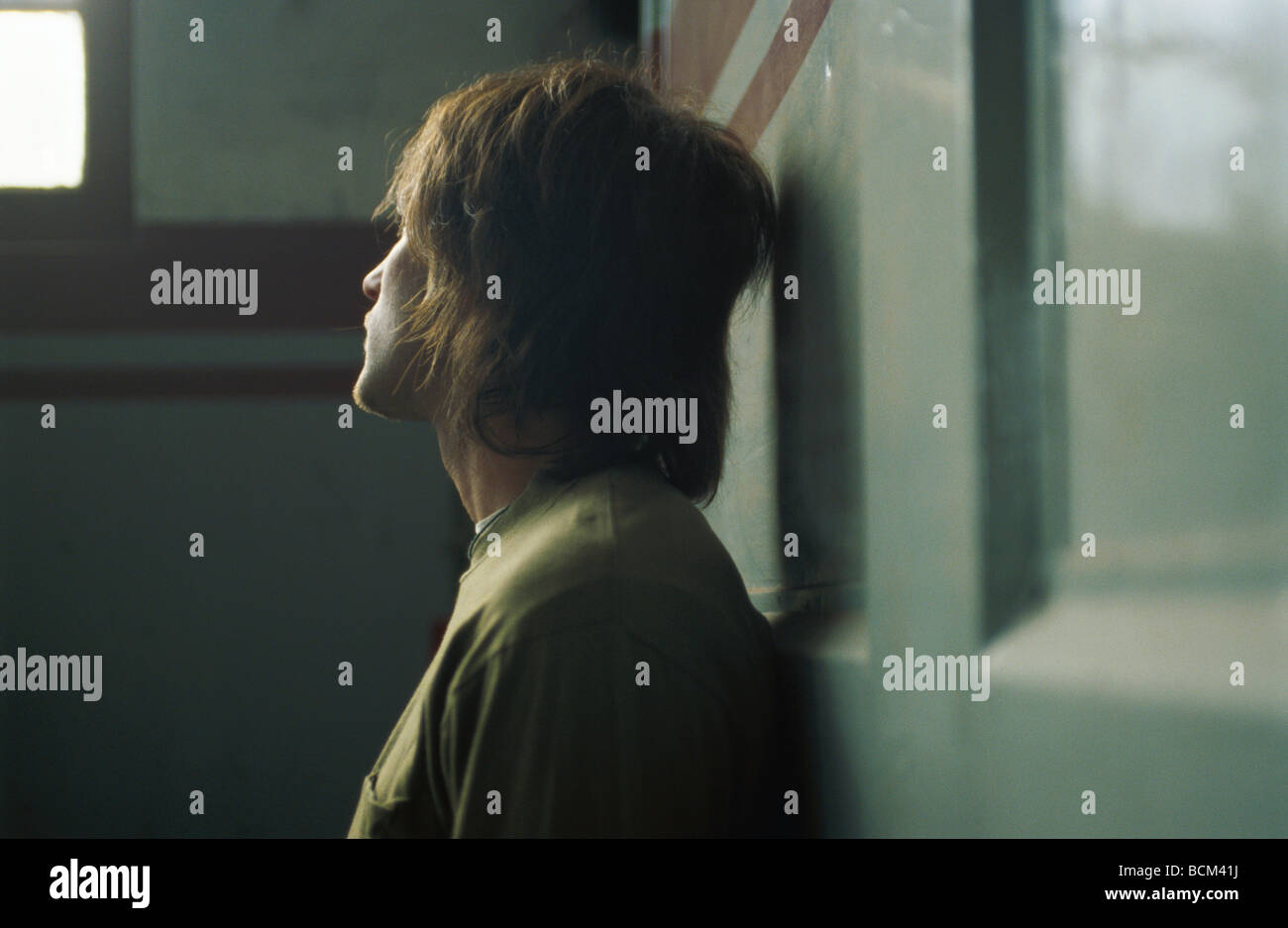 Young man leaning against wall, looking up at window Stock Photo - Alamy