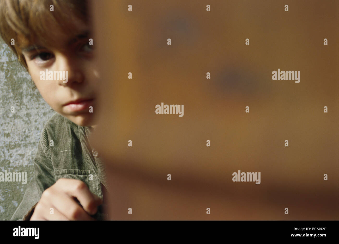 Boy looking around wall, focus on background Stock Photo - Alamy