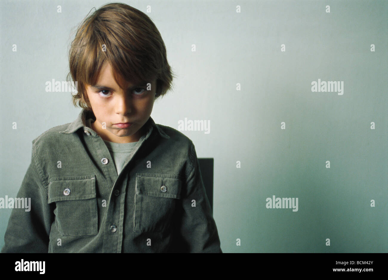 Boy frowning at camera, sitting in chair Stock Photo - Alamy