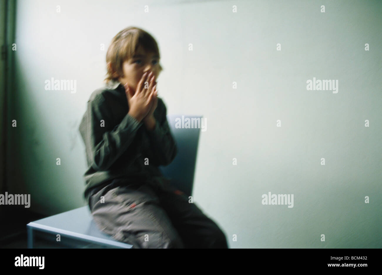 Boy sitting in chair with hands over his mouth Stock Photo - Alamy