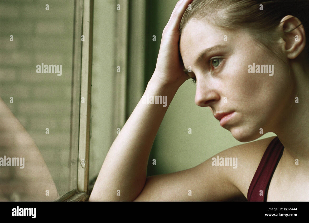 Young woman holding head and looking out window, side view Stock Photo ...