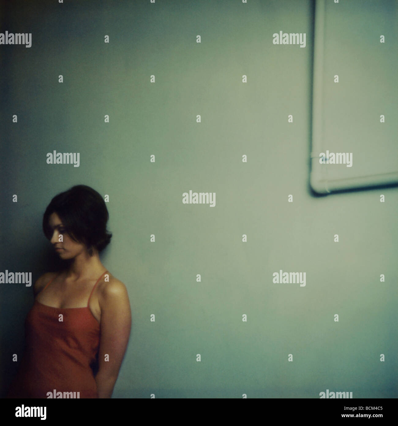 Young woman leaning against wall, looking down Stock Photo - Alamy
