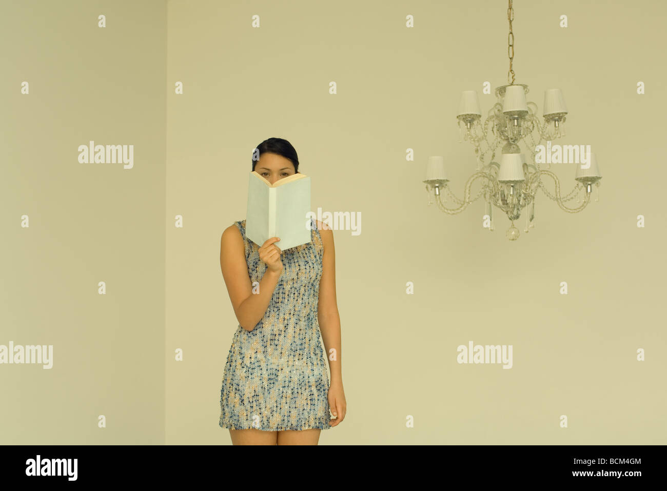 Woman standing beside chandelier, peeking over book at camera Stock ...