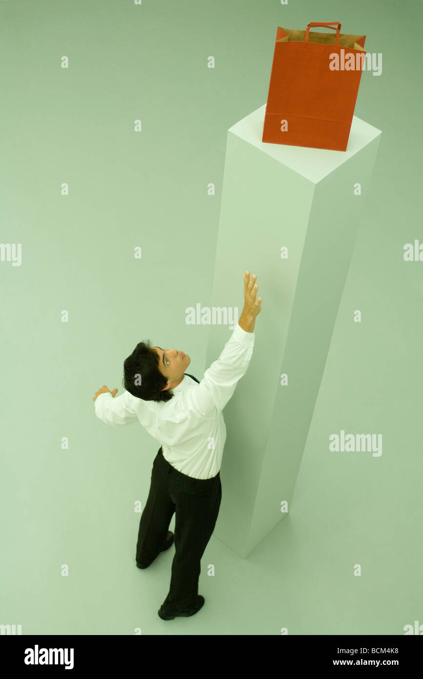 Man standing beside tall pedestal, reaching for shopping bag, high ...