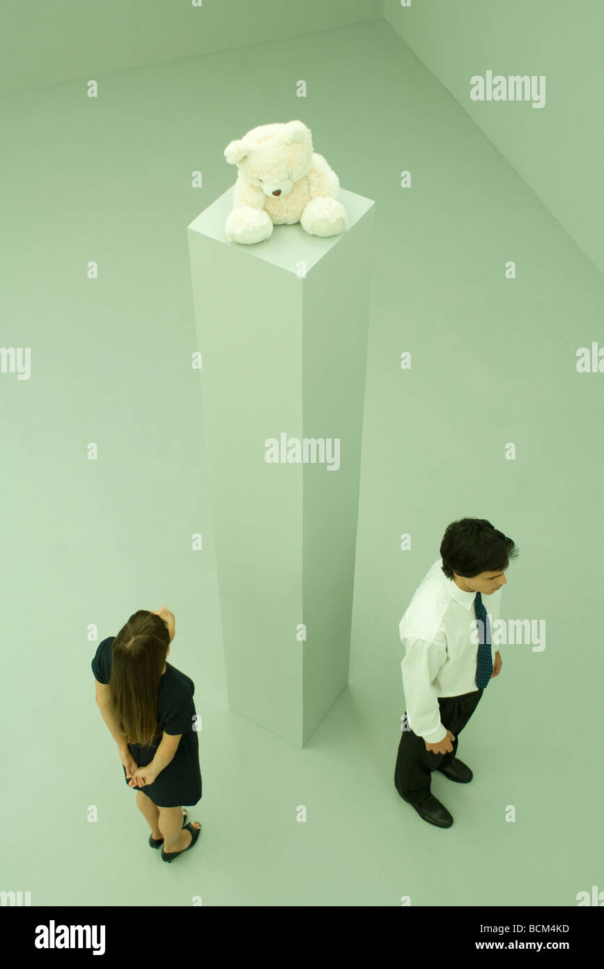 Man and woman standing beneath tall pedestal with teddy bear on top ...