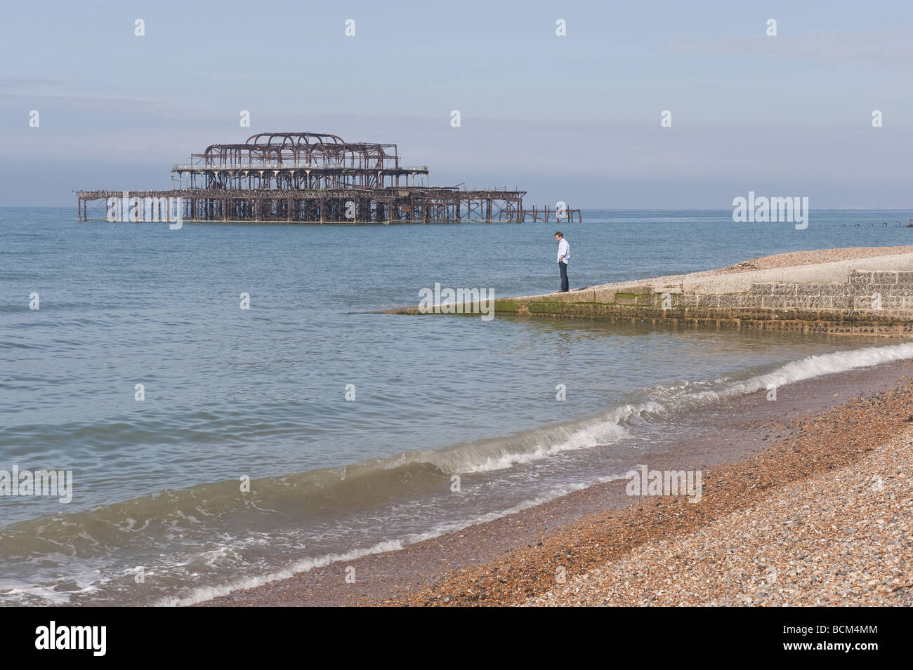 Solitary man looking out alone over sea and fire damaged pier from ...