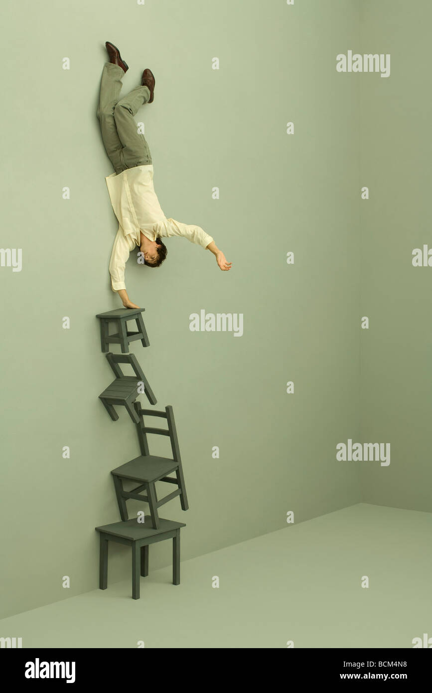 Man balancing on one hand on tall stack of chairs Stock Photo - Alamy