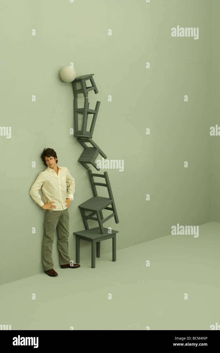 Man standing beside precariously stacked chairs, large ball about to ...