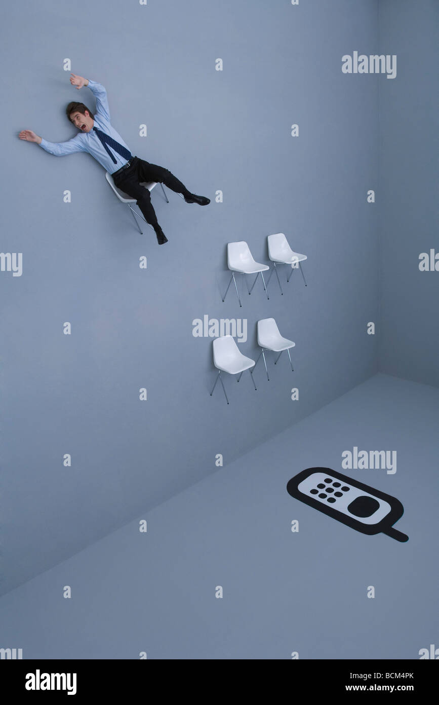 Man sitting in chair, falling towards other chairs arranged before ...