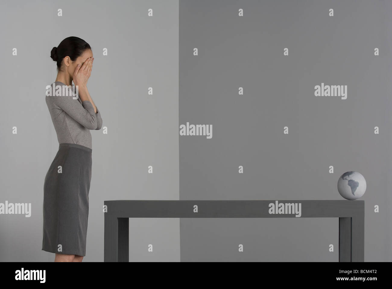 Woman standing beside table covering face with hands, globe set at ...