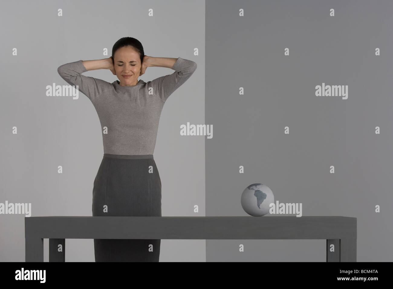 Woman standing behind table, hands over ears, eyes closed, small globe ...