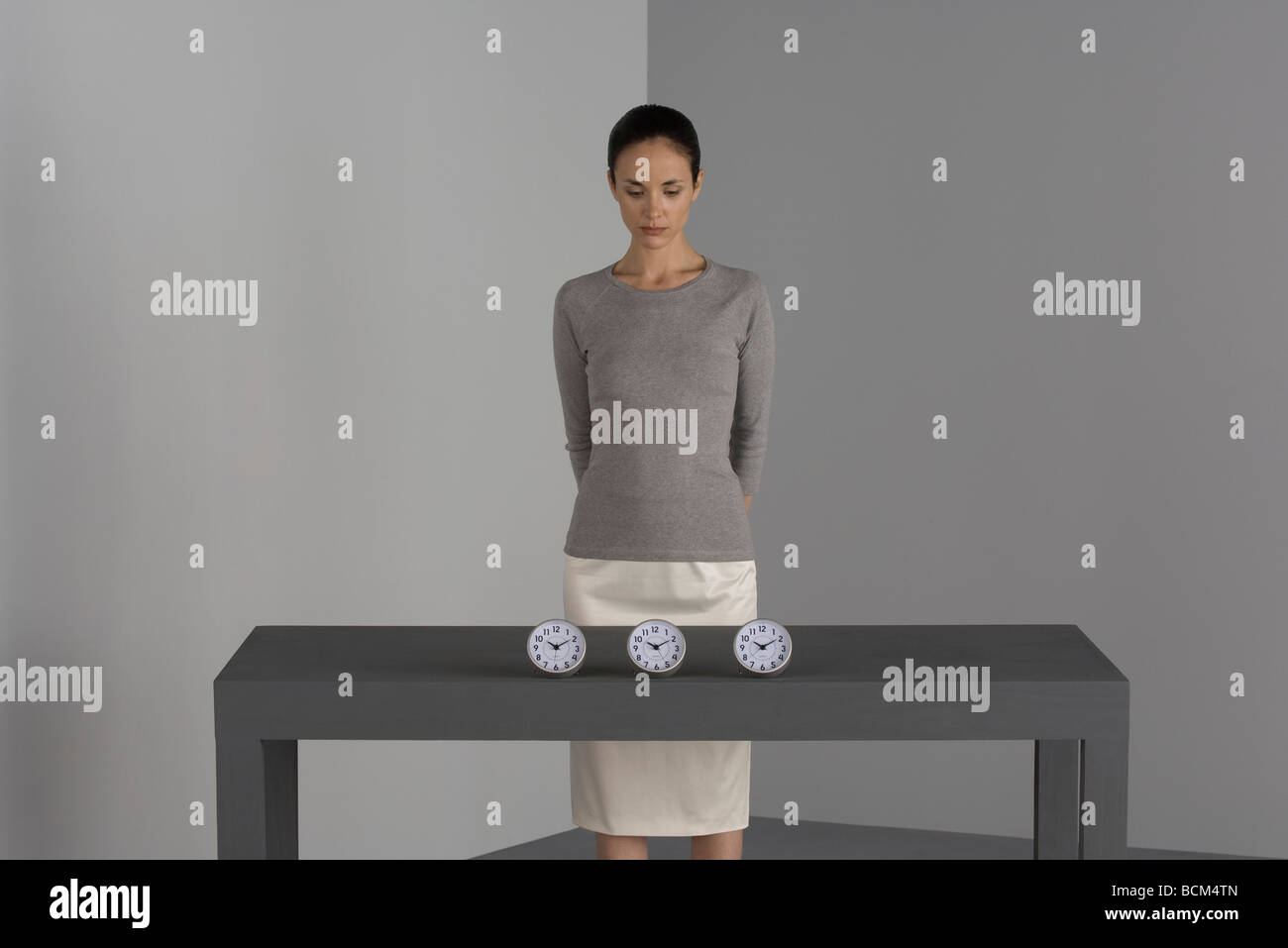 Woman standing behind table, looking down at row of clocks, hands ...