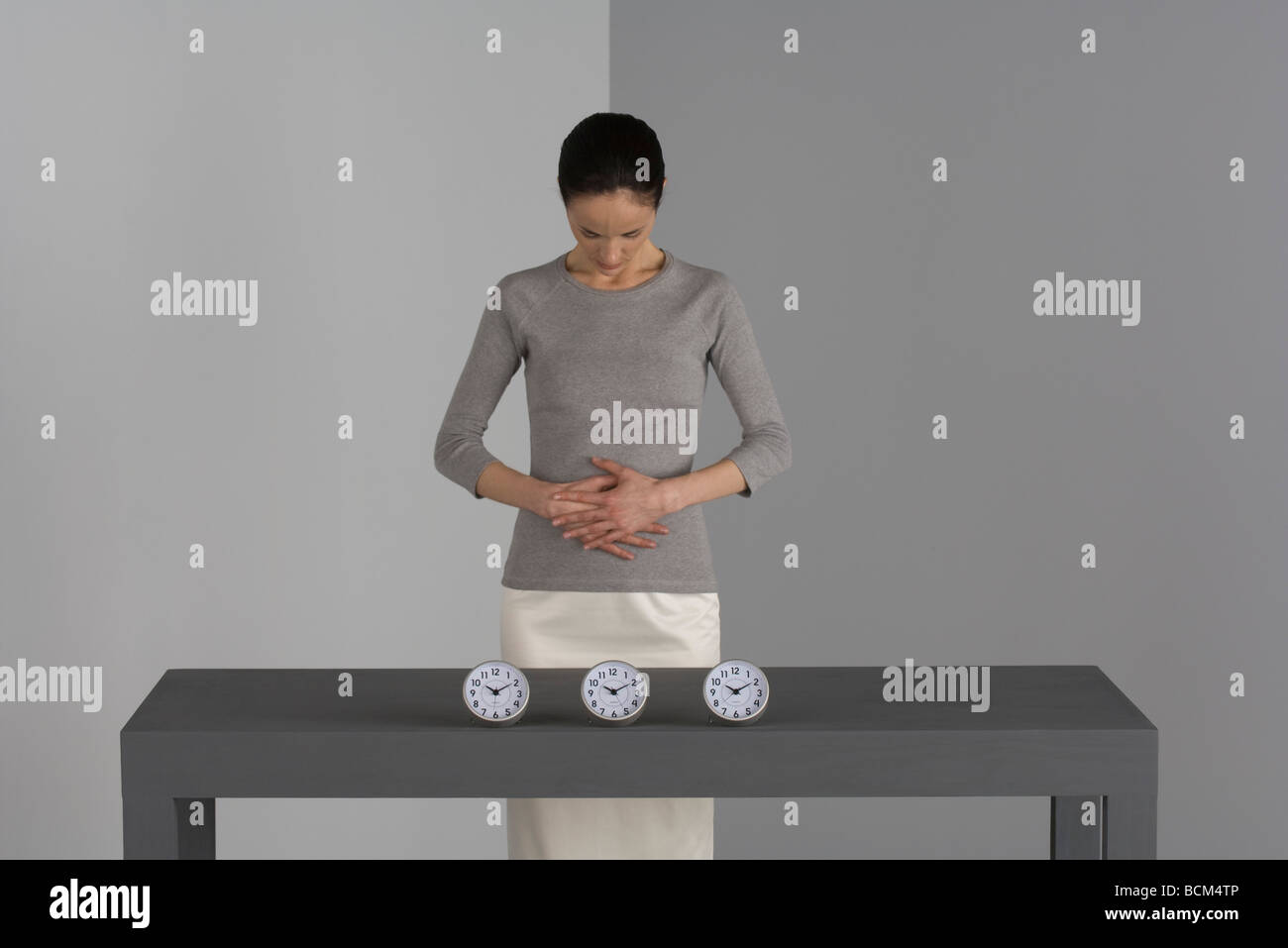 Woman standing with hands on stomach, looking down, clocks lined up in ...