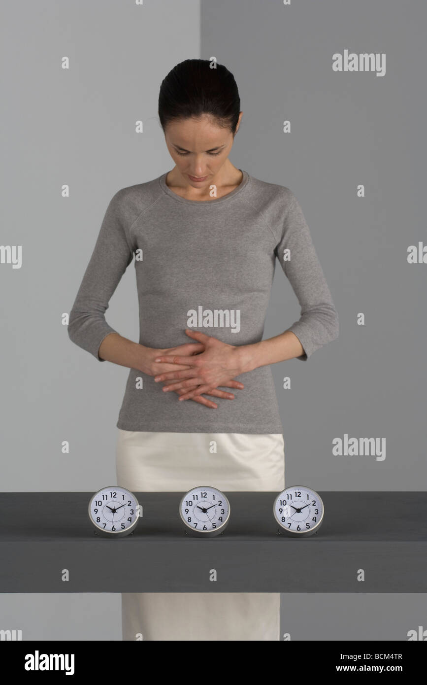 Woman standing with hands on stomach, looking down, clocks lined up in ...