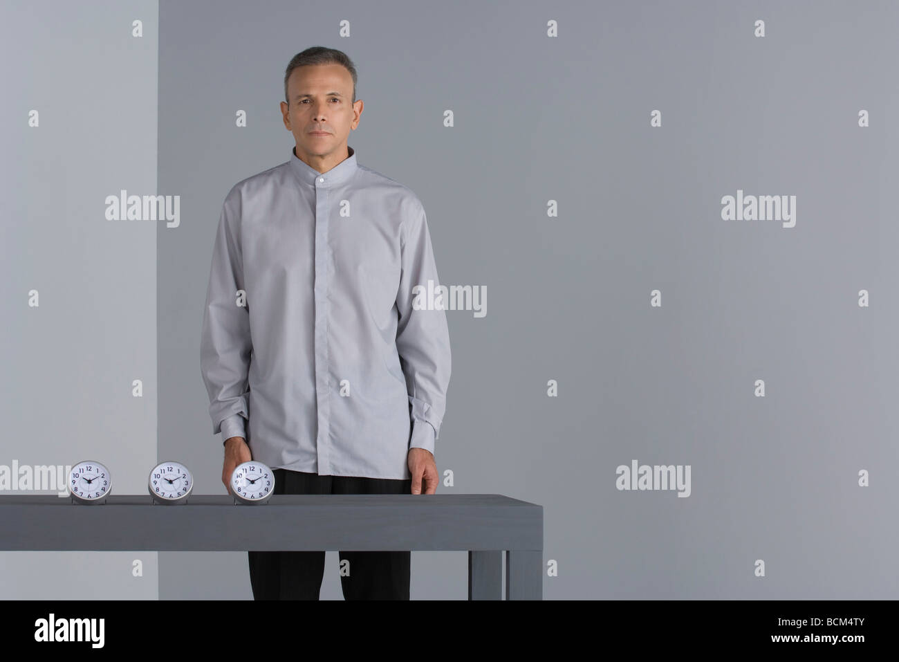 Man standing behind table with row of clocks, looking at camera Stock ...