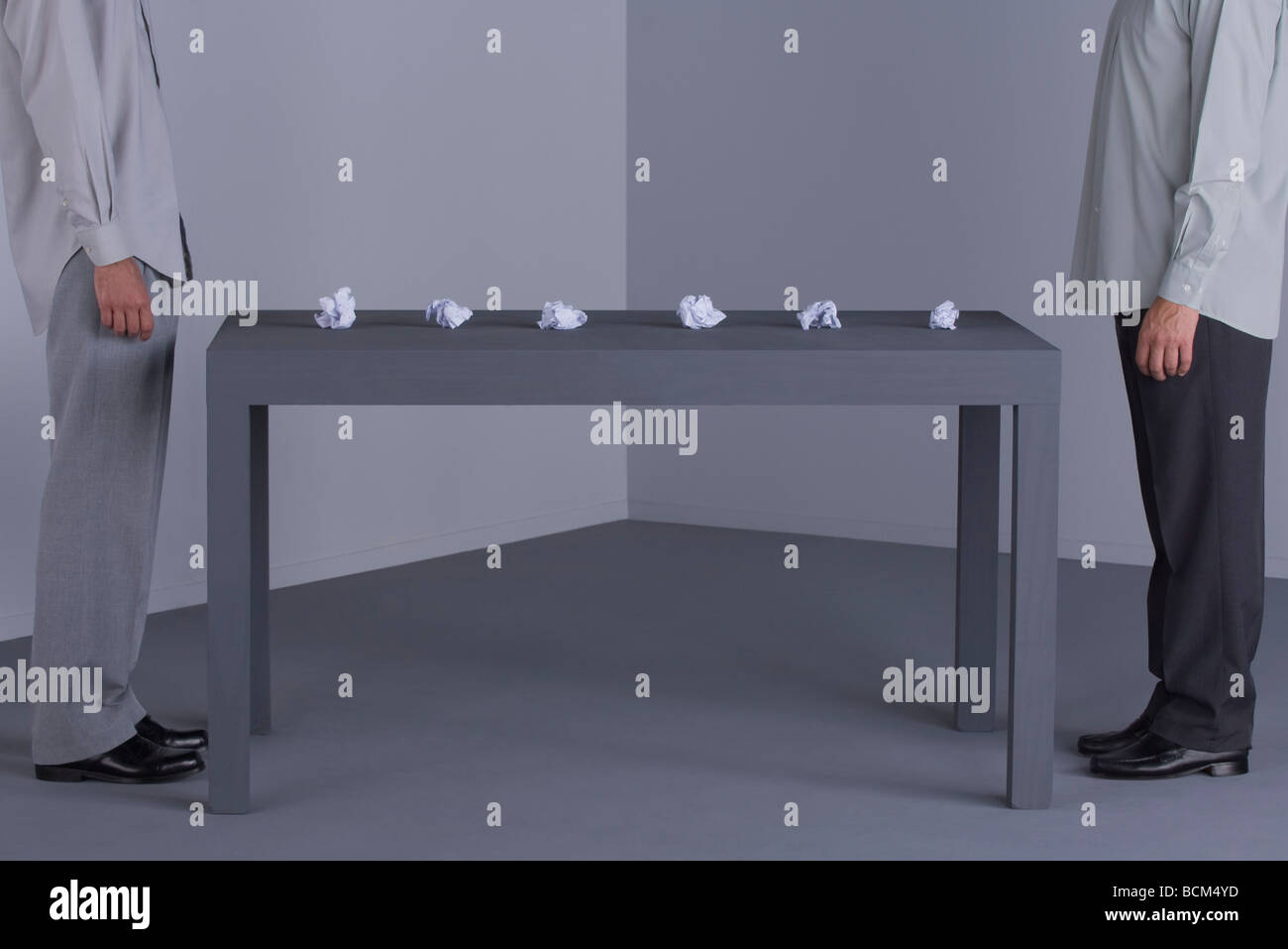 Two men standing at table with paper balls lined up between them, side ...