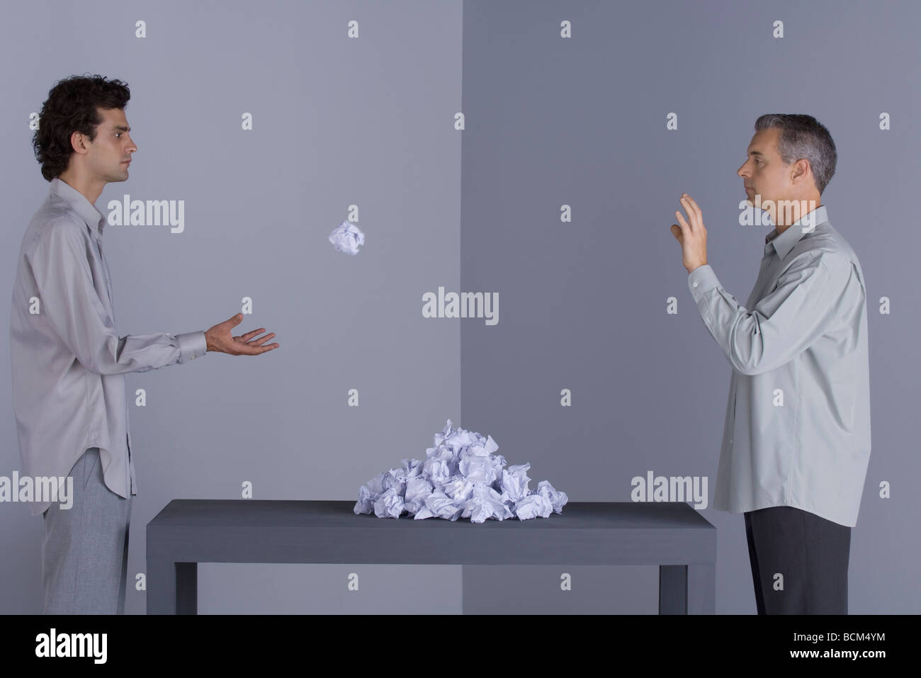Two men standing face to face, one throwing paper ball, pile of ...