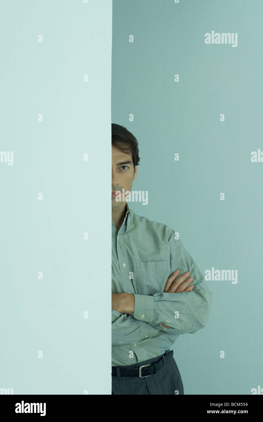 Man looking around corner, arms folded Stock Photo - Alamy